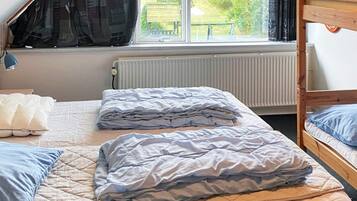 Quarto em dormitório com beliches, janela com cortinas, radiador e cama com colchão acolchoado.