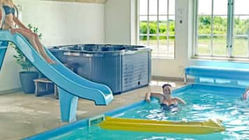 Piscina interna com escorrega, banheira de hidromassagem e vista para o verde lá fora.