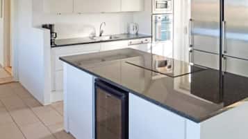 Cozinha moderna com armários brancos, bancada ilha em vidro, eletrodomésticos de aço inoxidável e lava-louças.