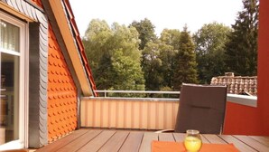 Um deck de madeira com mesa e cadeiras, um copo de suco de laranja e vista para árvores.