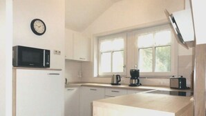 Cozinha compacta com armários brancos, micro-ondas, máquina de café e torradeira.