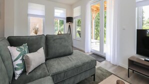 Uma sala de estar moderna com um sofá modular cinza, uma TV de tela plana em um suporte de madeira e uma grande porta de vidro deslizante que dá para um pátio.