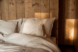 Cama com lençóis brancos em quarto com paredes de madeira.