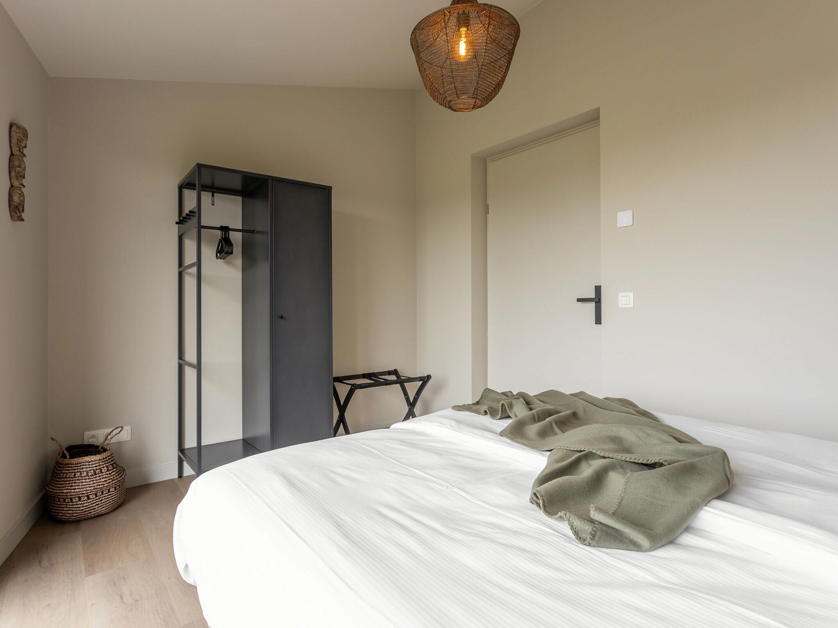 Um quarto com uma cama grande, um guarda-roupa, uma porta e um lustre.