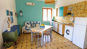 Uma cozinha compacta com mesa, cadeiras, máquina de lavar e sofá.