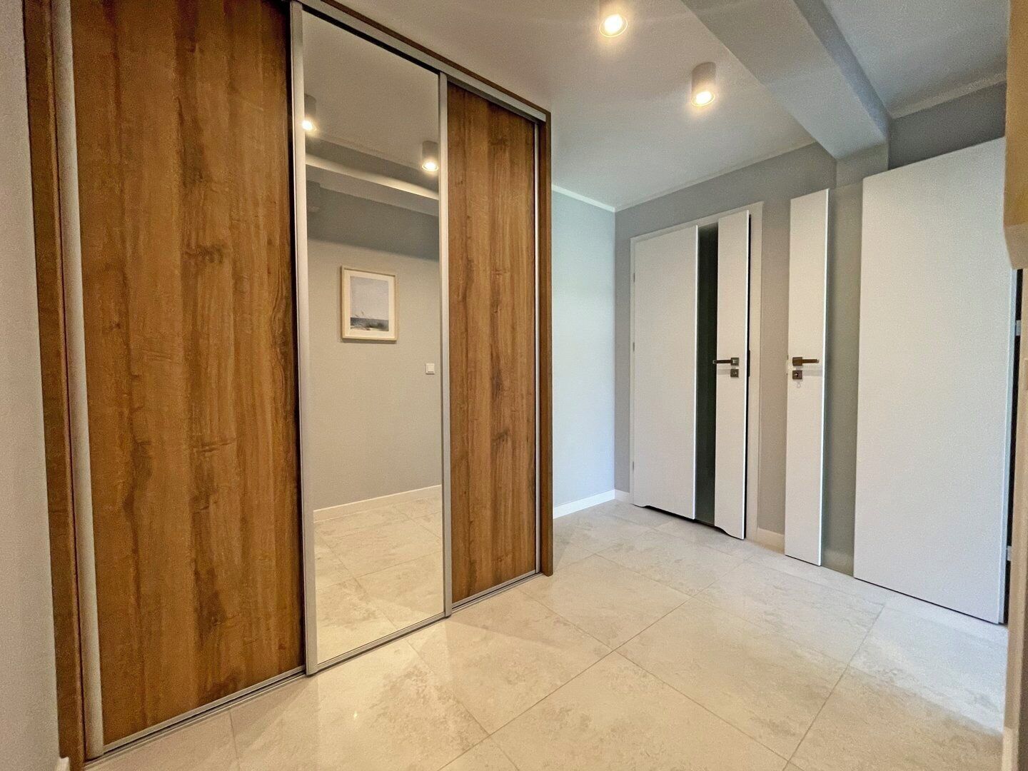 Um corredor com porta deslizante, quadro emoldurado na parede e chão revestido de azulejos.