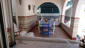 Uma área de refeições com uma mesa posta para quatro pessoas, cercada por paredes estampadas e um chão de azulejos.