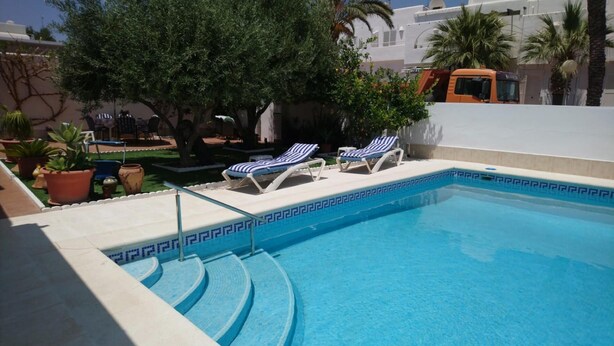Uma piscina com azulejos azuis, duas espreguiçadeiras e plantas em vasos.