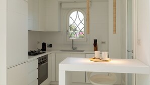 Cozinha moderna com armários brancos, fogão a gás, pia e janela com detalhes decorativos.