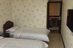 Quarto de hotel com duas camas, cabeceira de madeira, televisão na parede e porta para um banheiro.