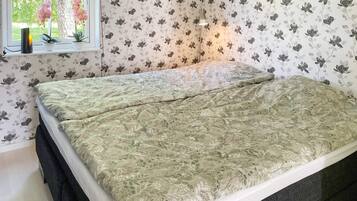 Quarto com cama, papel de parede floral, janela com plantas e relógio de parede.