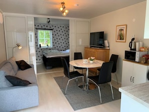 Um espaço compacto com cama, sofá, mesa de jantar com cadeiras, televisão e cozinha compacta.