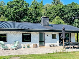 Uma casa moderna com telhado cerâmico, varanda coberta com móveis de exterior e área de jardim.
