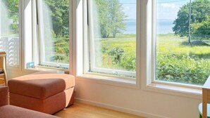 Quarto com uma janela ampla que dá para uma área gramada e árvores, um sofá rosa e piso de madeira.