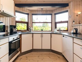 Cozinha moderna com armários de madeira, forno embutido, máquina de café e vista para o verde através de grandes janelas.