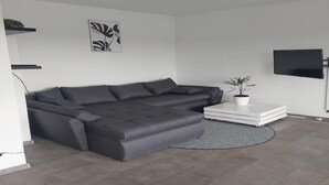 Uma sala de estar moderna com um sofá modular cinzento, uma mesa de centro branca e um vaso com planta.