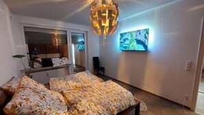 Quarto moderno com uma cama grande, ventilador de teto, televisão e janela com vista para uma varanda.