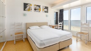 Quarto de hotel com cama, escrivaninha, cadeira e vista para a praia.