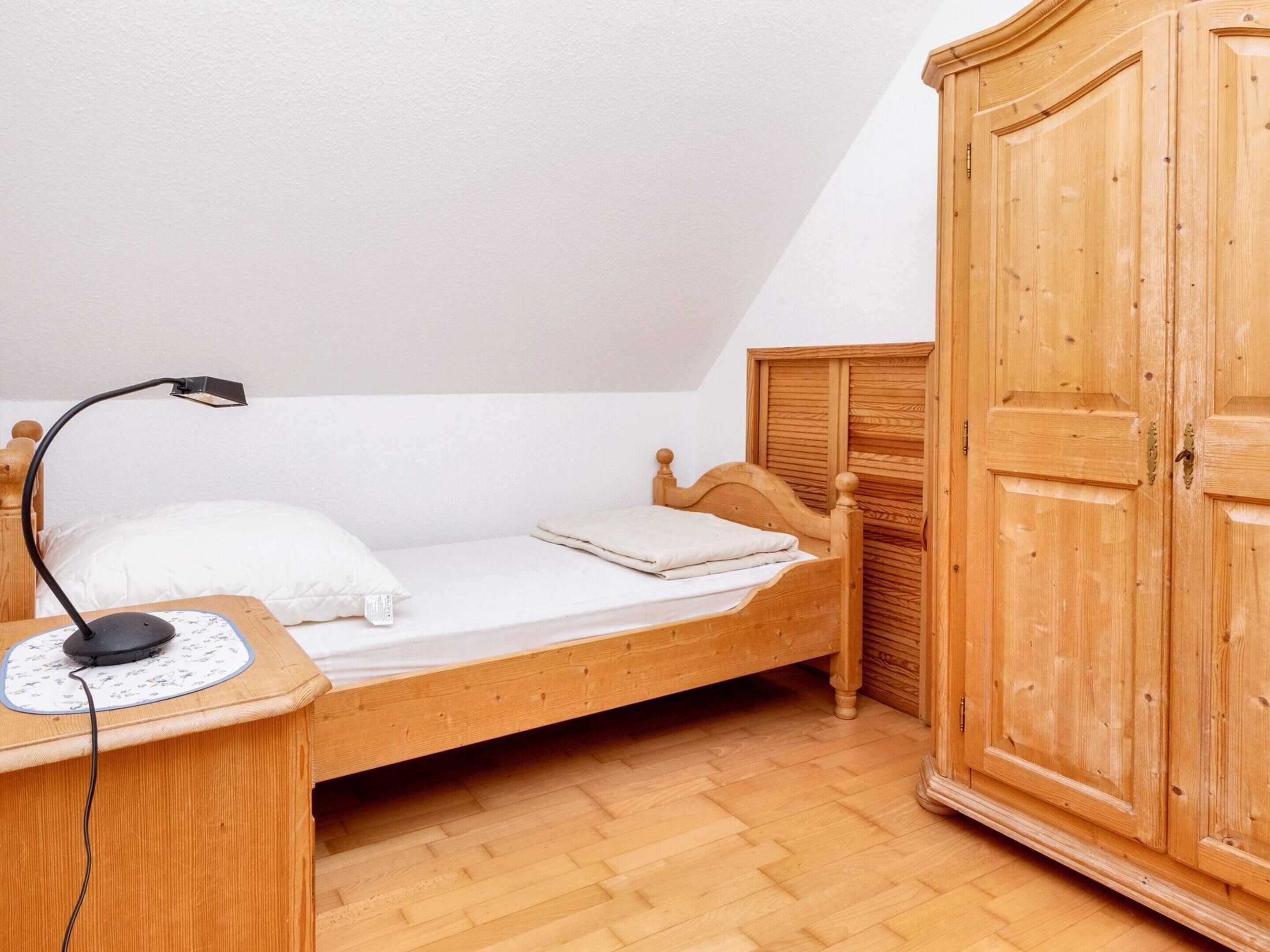 Uma cama de solteiro com cabeceira de madeira, uma mesa de cabeceira com abajur e um guarda-roupa.