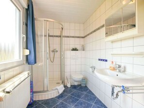 Casa de banho com chuveiro, sanita e lavatório, com azulejos brancos e chão azul.