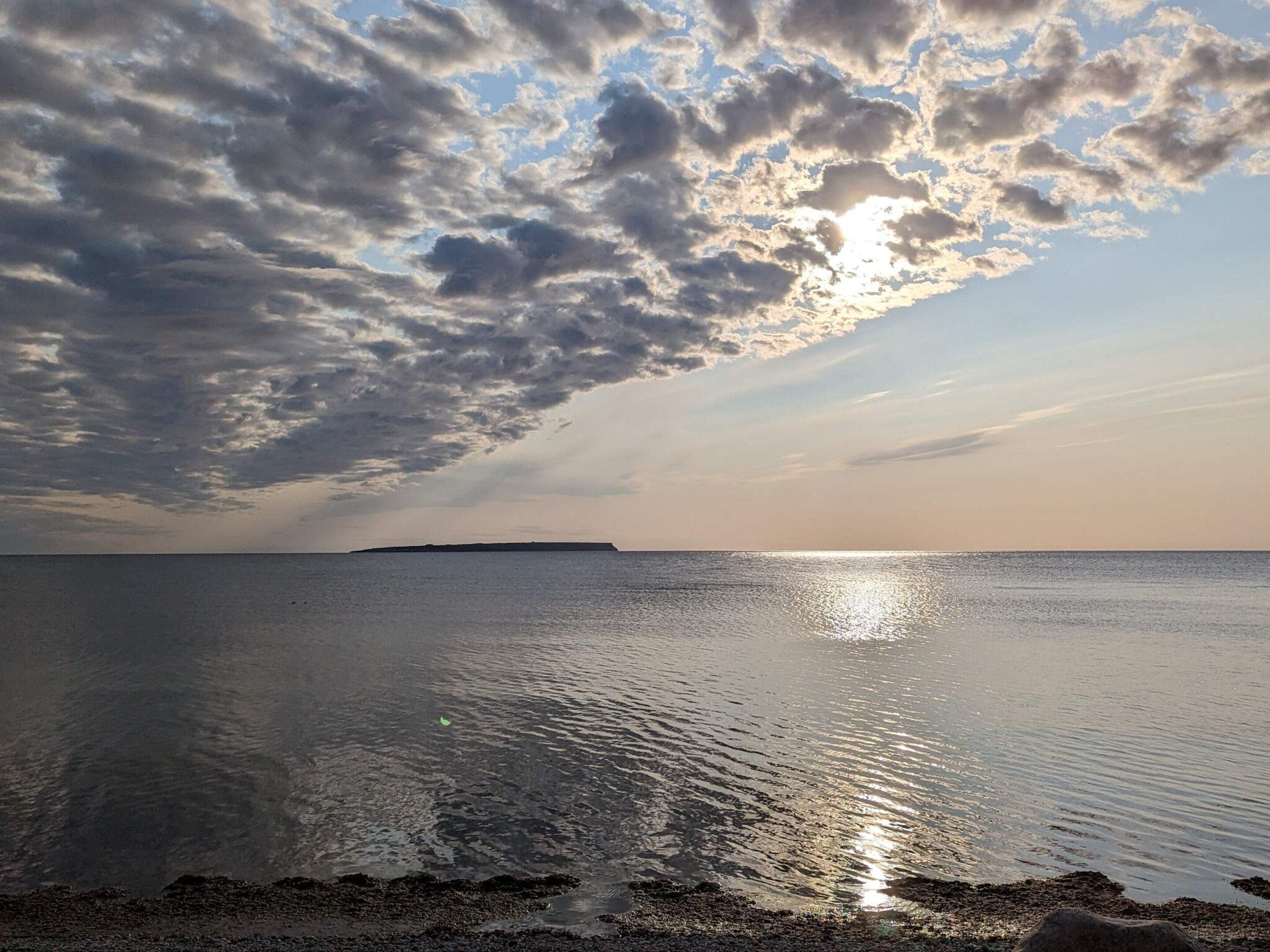Mar calmo com uma terra distante sob céu nublado.