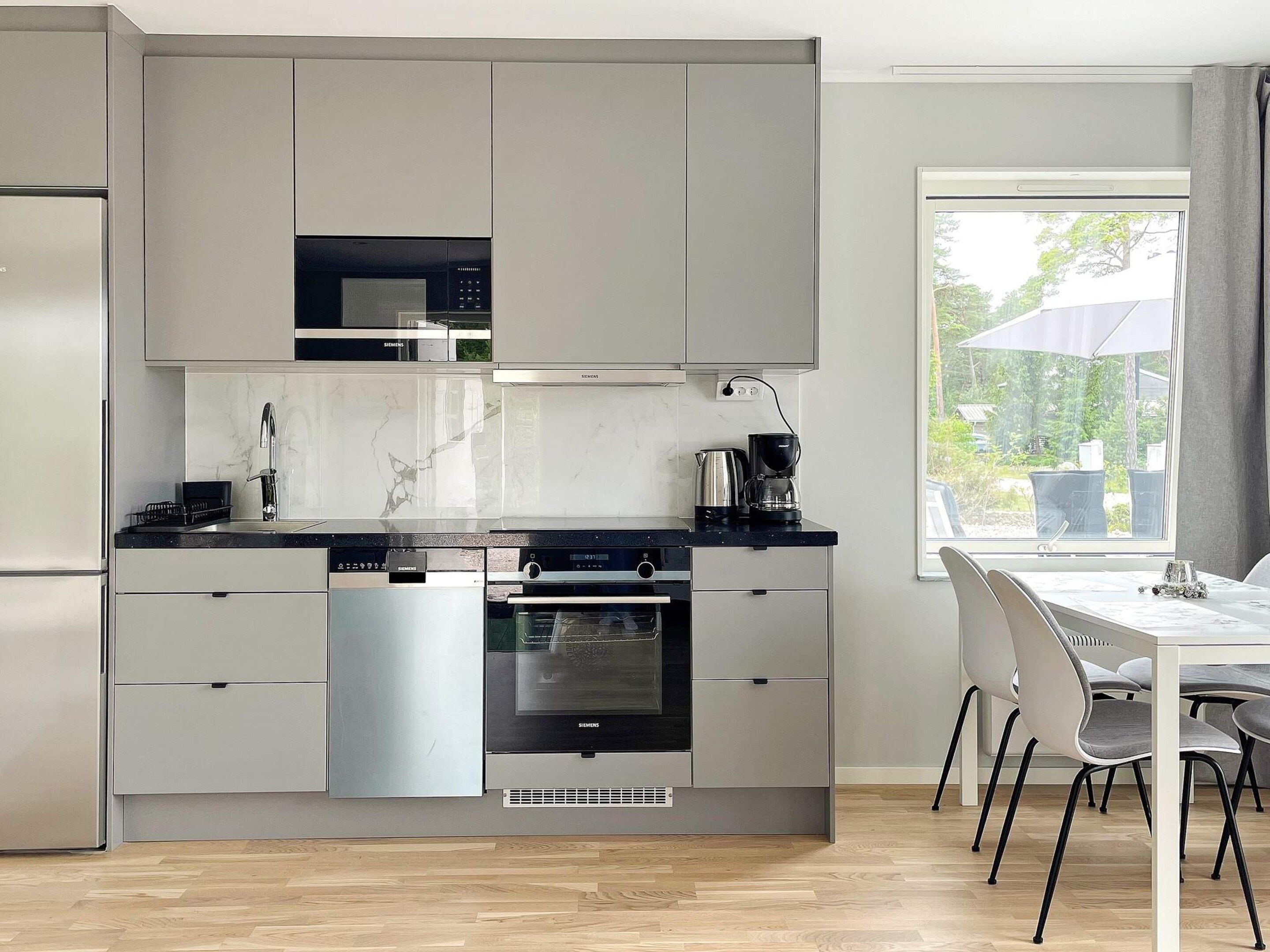 Cozinha moderna com eletrodomésticos integrados, sala de jantar com mesa e cadeiras, e janela com vista para áreas verdes.