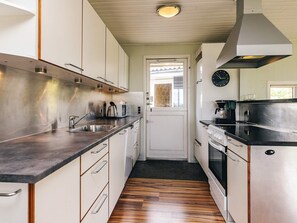 Cozinha compacta com eletrodomésticos de aço inoxidável, bancada preta e piso de madeira.