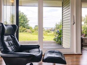 Quarto com poltrona e apoio para os pés de couro preto, porta de correr de vidro que dá para um jardim e vista para o mar.