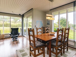 Uma área de refeições com mesa e cadeiras de madeira, um mapa na parede e grandes janelas com vista para o exterior.
