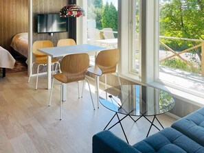 Sala de estar moderna com mesa de vidro, piso de madeira e uma grande janela com vista para o verde.