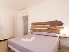 Quarto com cama, mesa de cabeceira com luminária e bandeja com itens de café da manhã.