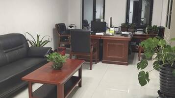 Uma sala de estar mobiliada com sofá, mesa de centro de madeira, escrivaninha com computador e plantas em vasos.