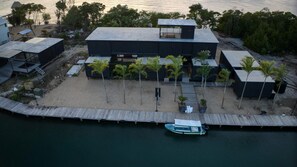 Uma propriedade costeira moderna com um cais, área de praia com palmeiras e um barco.