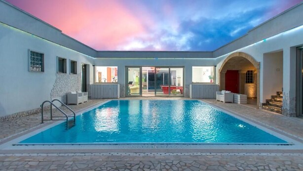Piscina interior com paredes de vidro transparente, piso de ladrilho de pedra e vista do céu pelo teto.