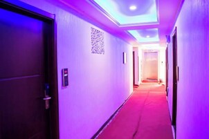 Corredor de hotel com carpete vermelho, um código QR na parede e uma porta à esquerda.