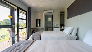 Quarto de hotel com duas camas, banheiro e varanda com cadeiras.