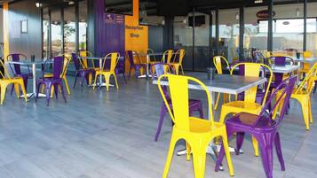 Uma área de recepção com cadeiras e mesas em roxo e amarelo, um balcão de recepção e um aviso indicando que o acesso é reservado.