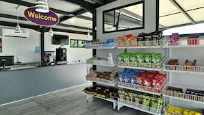 Interior de loja com prateleiras repletas de diversos snacks e um aviso de 'Welcome' acima do balcão.