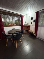 Uma sala de jantar com mesa redonda e quatro cadeiras, lareira de tijolos e janela com cortinas.