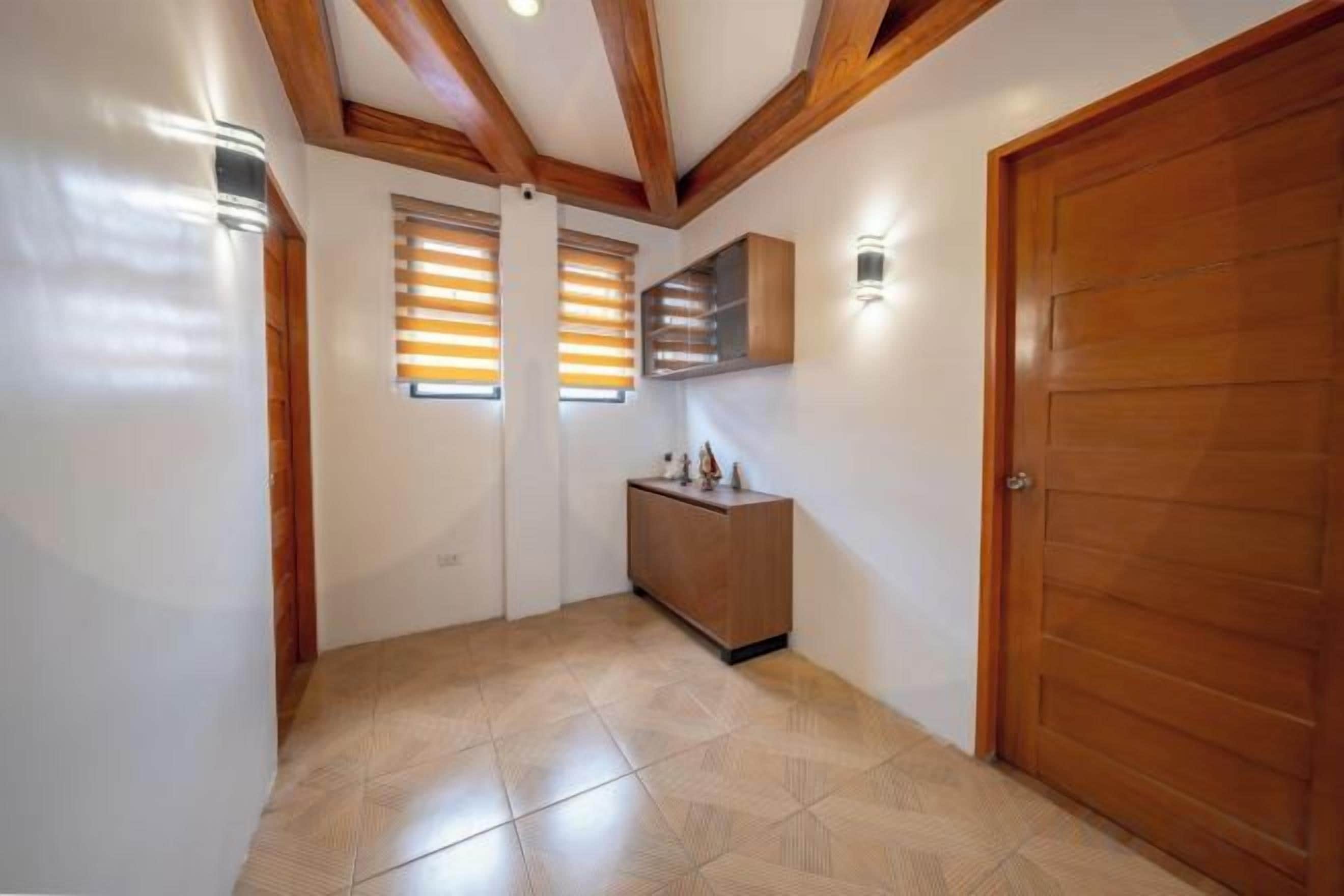 Um corredor com porta de madeira, um armário e duas janelas com persianas.