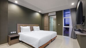 Quarto de hotel moderno com uma cama grande, mesas de cabeceira, uma televisão e vista para o exterior.