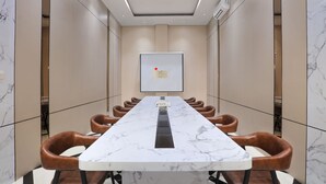 Uma sala de conferências com uma mesa comprida, cadeiras de couro marrom, uma tela de projetor e piso de mármore.