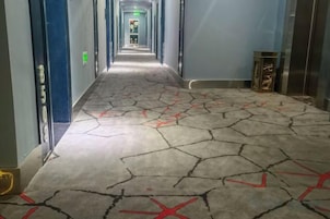 Um corredor com carpete estampado, portas em ambos os lados e um cesto de lixo à direita.