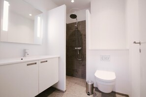 Um banheiro moderno com toucador branco, vaso sanitário e área de chuveiro.