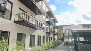 Um edifício residencial de vários andares com varandas, um caminho pavimentado e uma fileira de vasos com plantas.