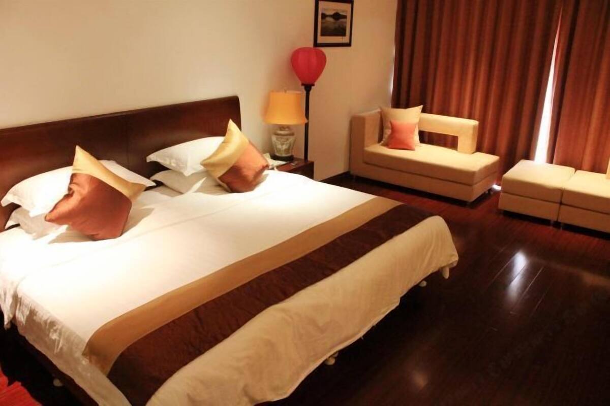 Quarto de hotel com uma cama grande, mesa de cabeceira com abajur, sofá e um balão vermelho decorativo.