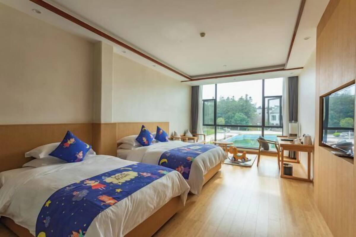 Quarto de hotel com duas camas, uma escrivaninha e vista para uma piscina.
