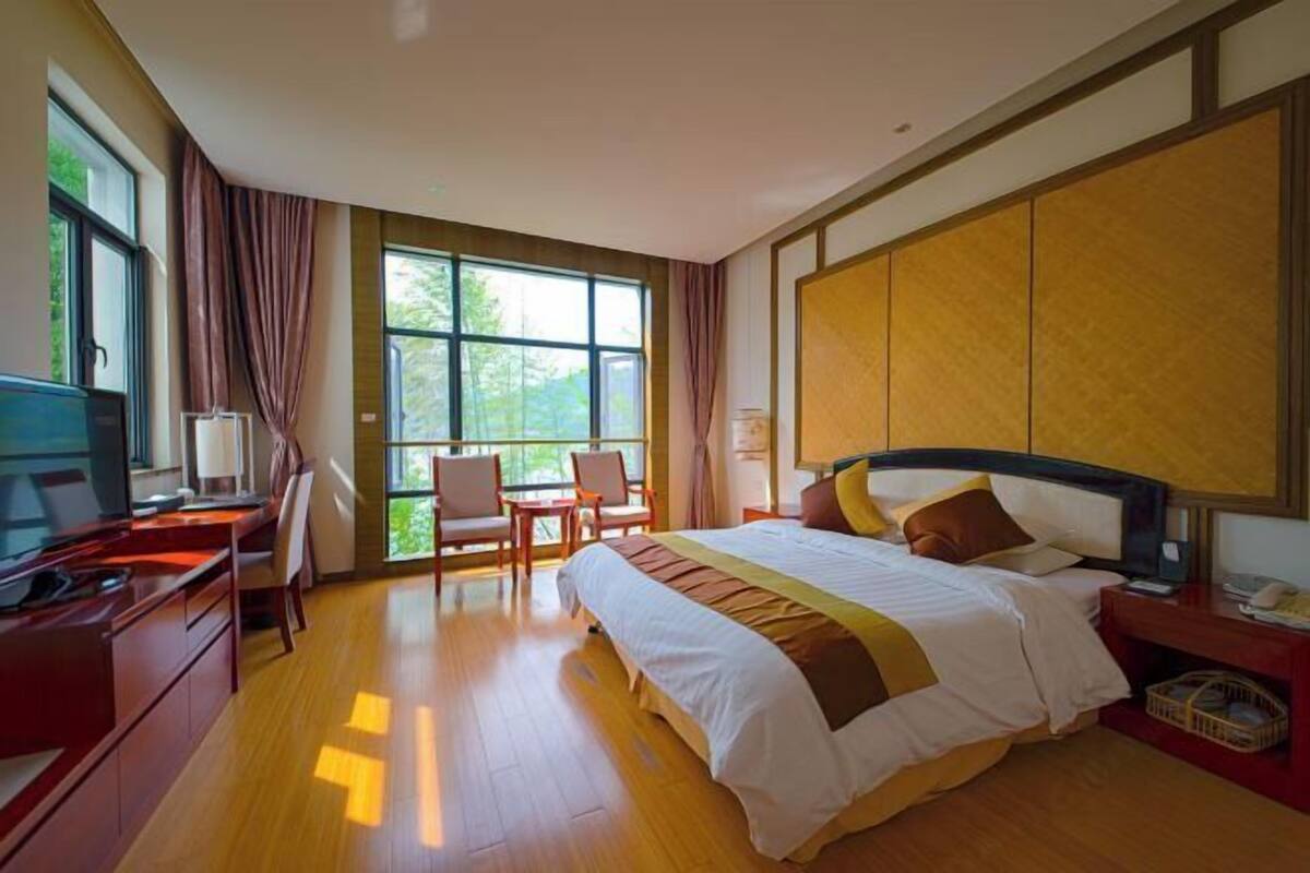 Quarto de hotel com uma cama grande, uma escrivaninha com computador, uma cadeira e uma televisão.