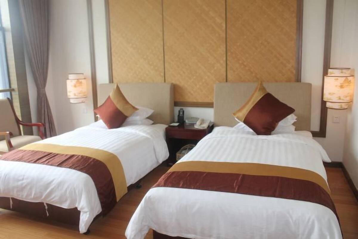 Quarto de hotel com duas camas, uma mesa de cabeceira, uma luminária e uma cortina.