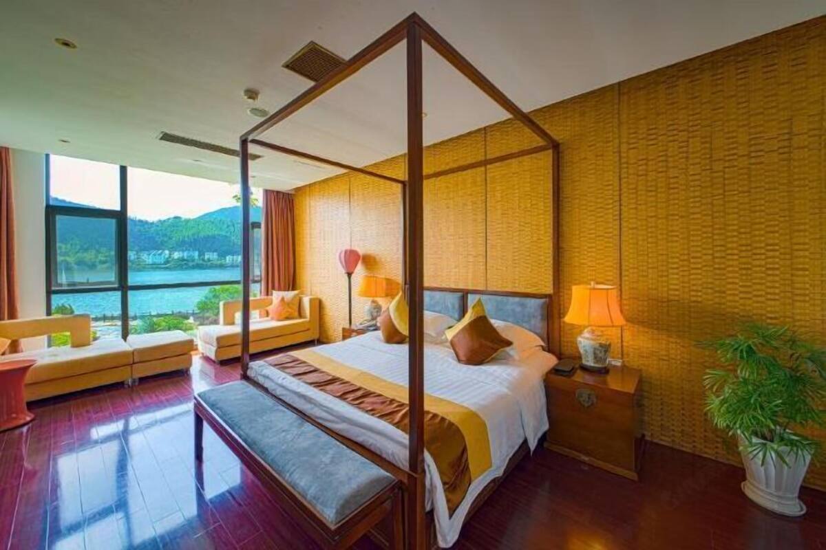Uma cama com dossel com vista para o mar, uma área de estar com sofá e poltronas, e uma grande planta em vaso.